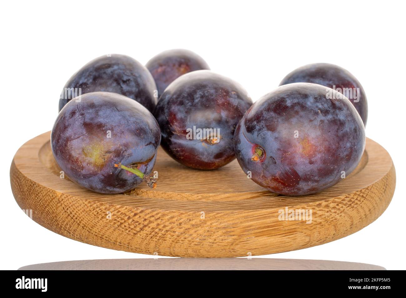 Several organic plums on a round wooden tray, close-up, isolated on a ...