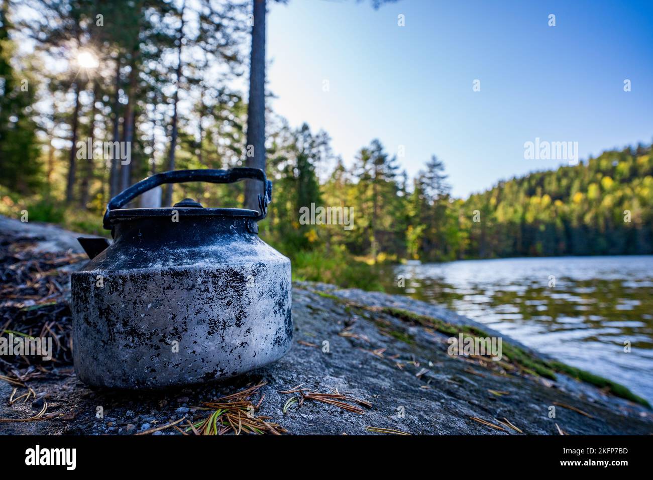 An old classic metal tea kettle set on the ground by a river in the ...