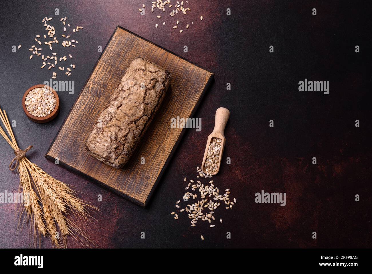 A loaf of brown bread with grains of cereals on a wooden cutting board ...