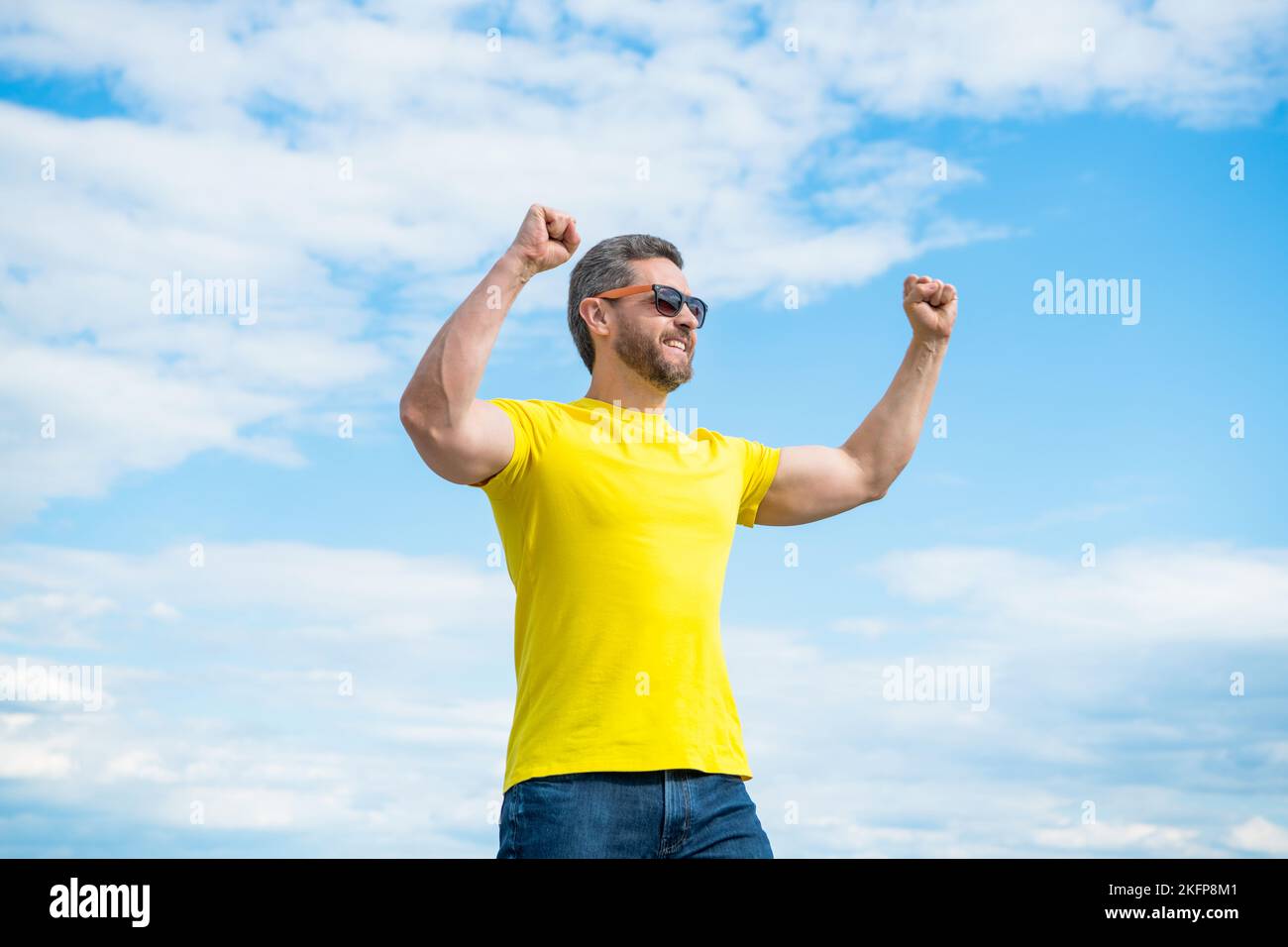 cheerful muscular man in yellow shirt and sunglasses on sky background ...
