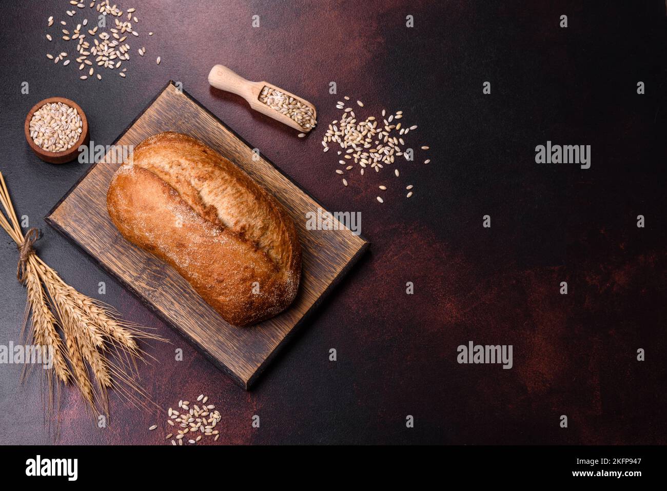 A loaf of brown bread with grains of cereals on a wooden cutting board ...