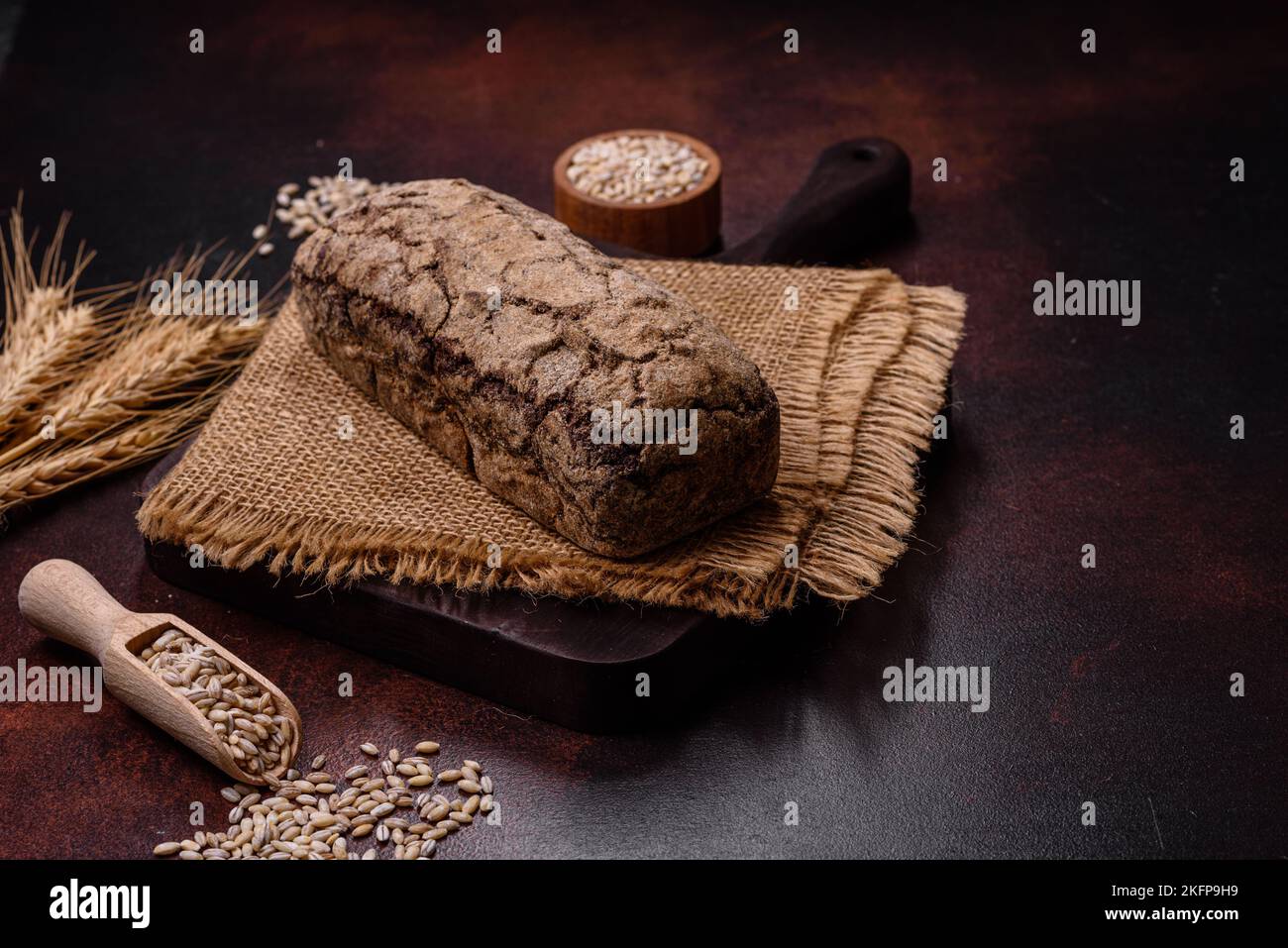A loaf of brown bread with grains of cereals on a wooden cutting board ...