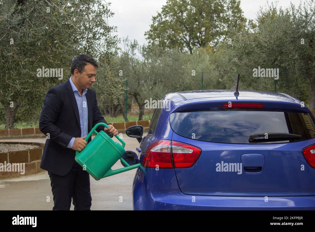 Image of an elegant man pouring water into the car tank with a ...