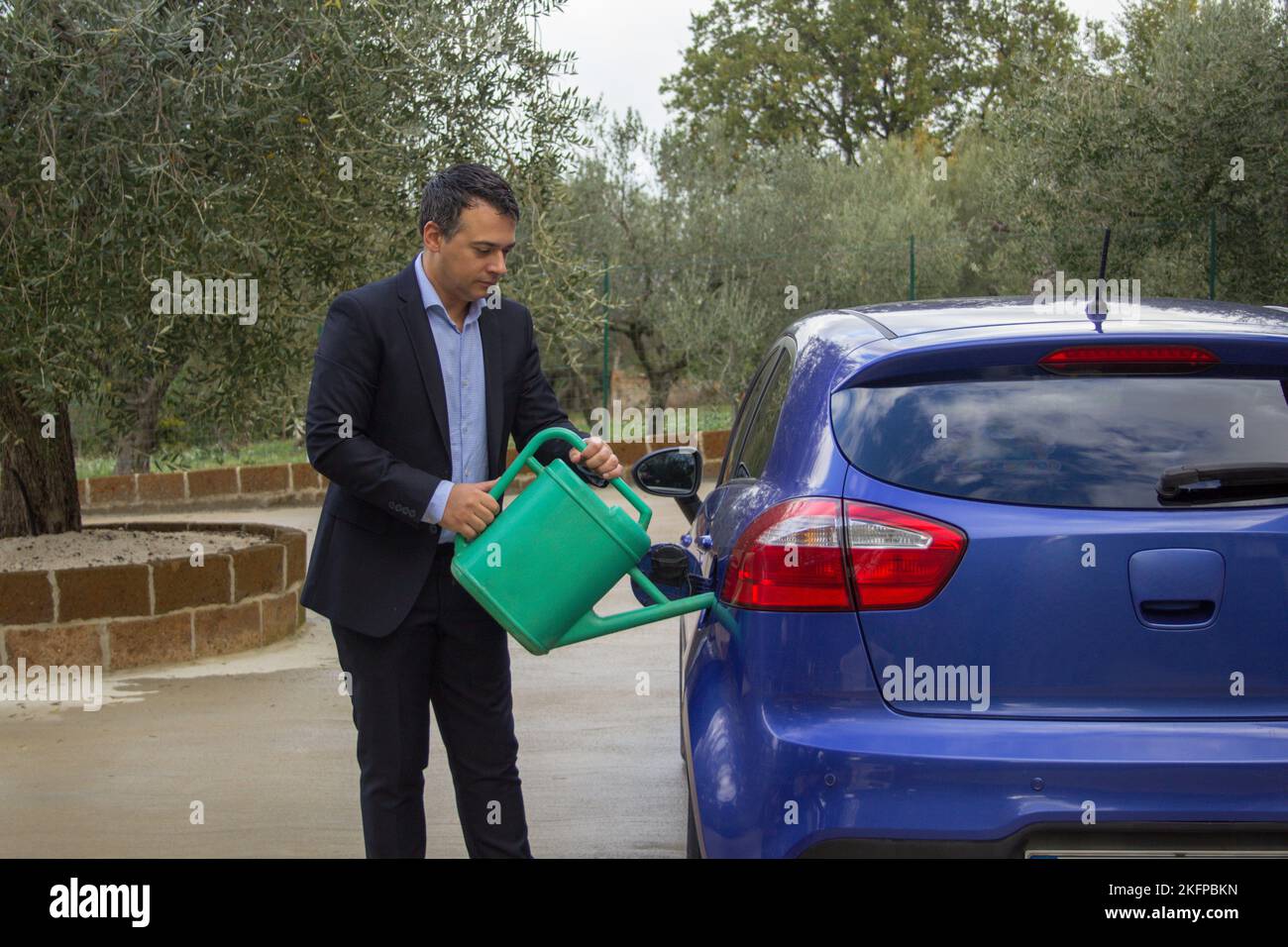 Image of an elegant man pouring water into the car tank with a ...