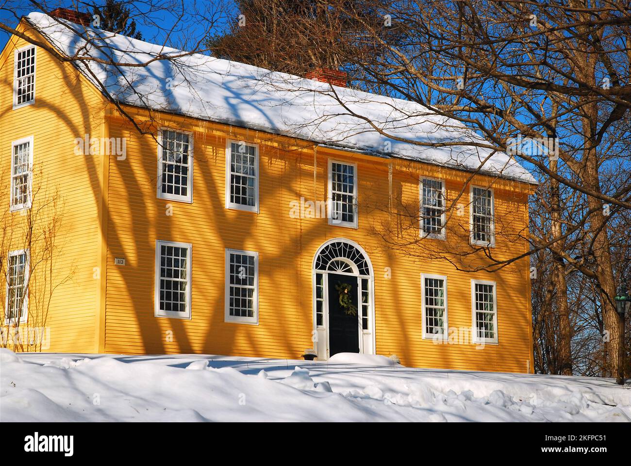 A quaint New England yellow house sits in a yard covered in winter snow ...