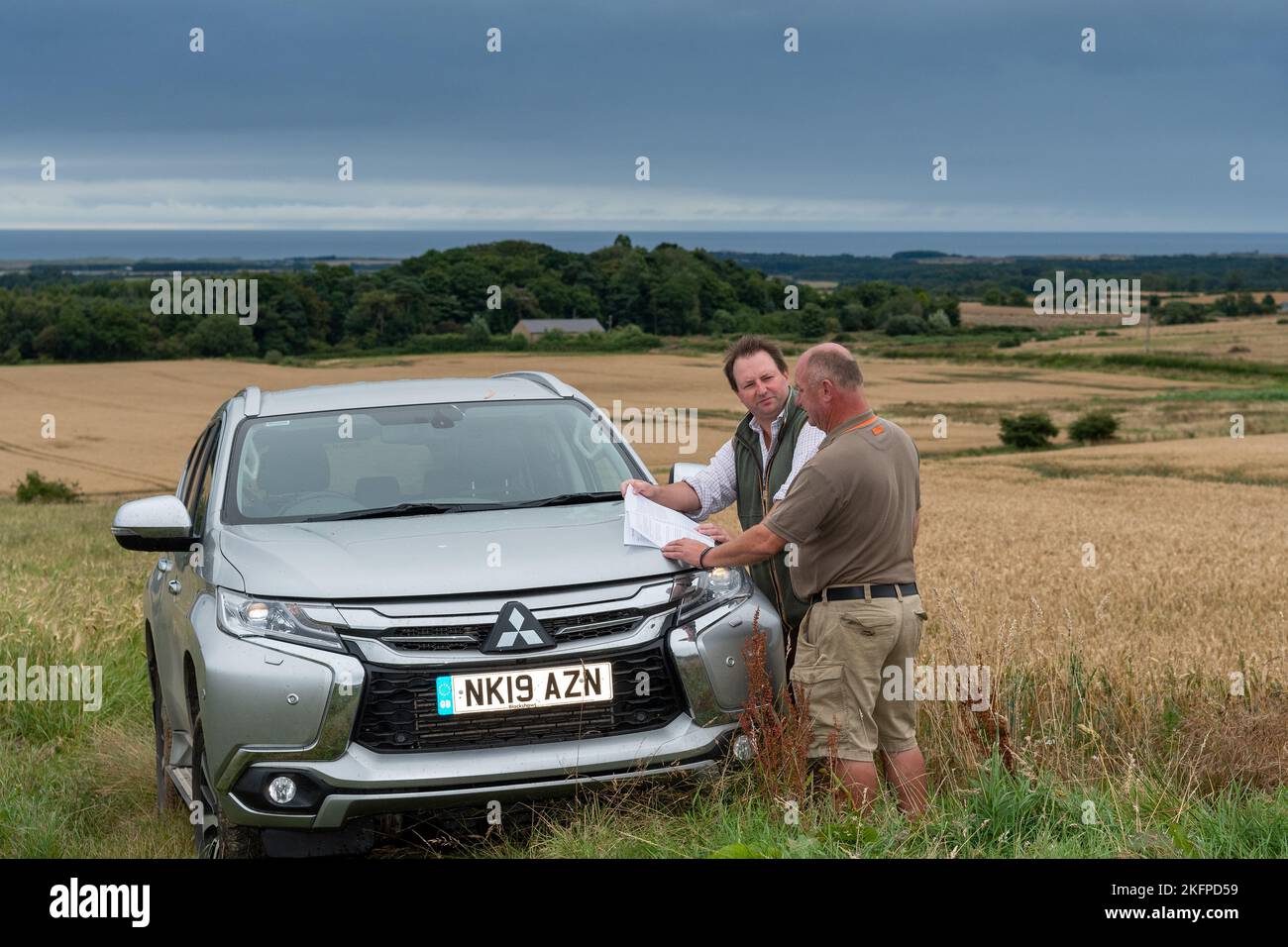 Land agent and farmer, leaning on a pickup, discussing farm management ...