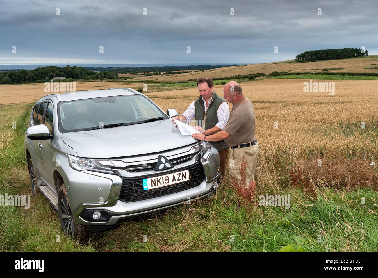 Land agent and farmer, leaning on a pickup, discussing farm management ...