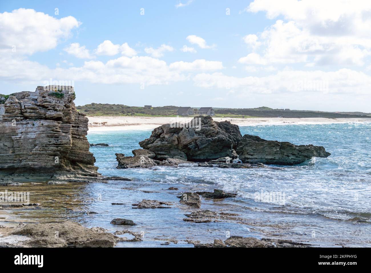A bright seascape of blue waves crashing against the rocks with a beach ...