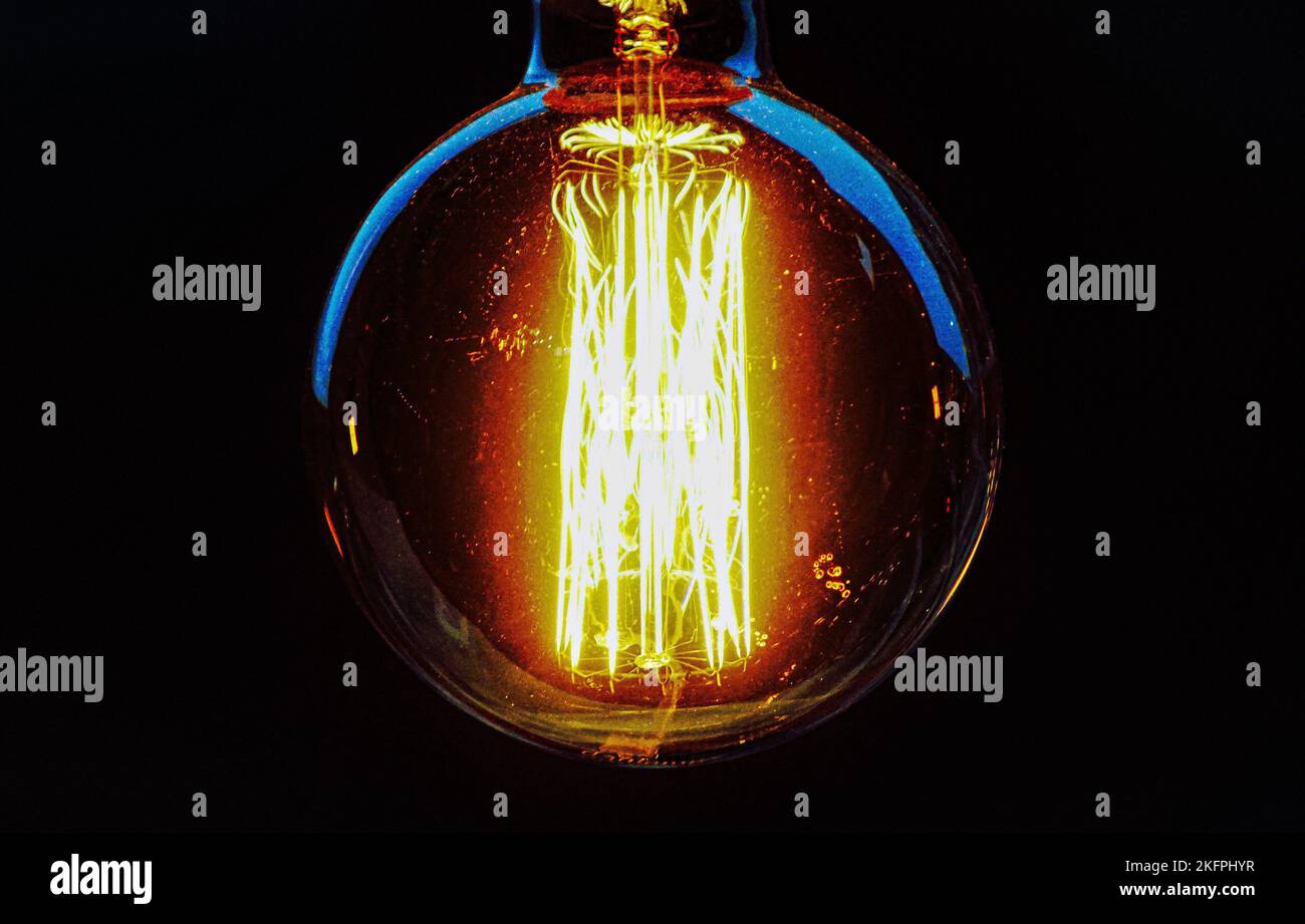 A closeup of a light bulb with bright yellow filament isolated on black ...