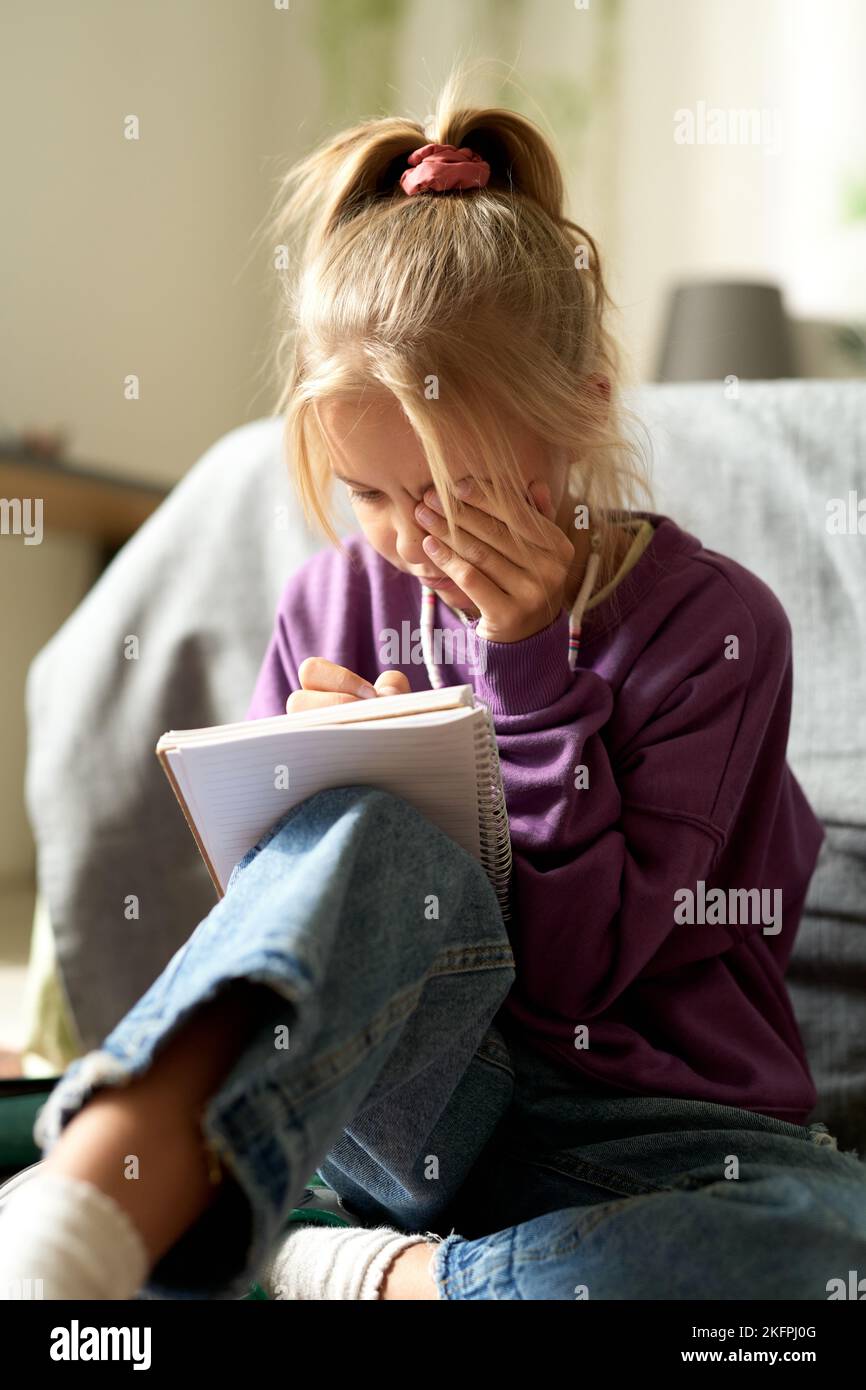 Sad little girl writing her emotions in diary wiping her tears with ...