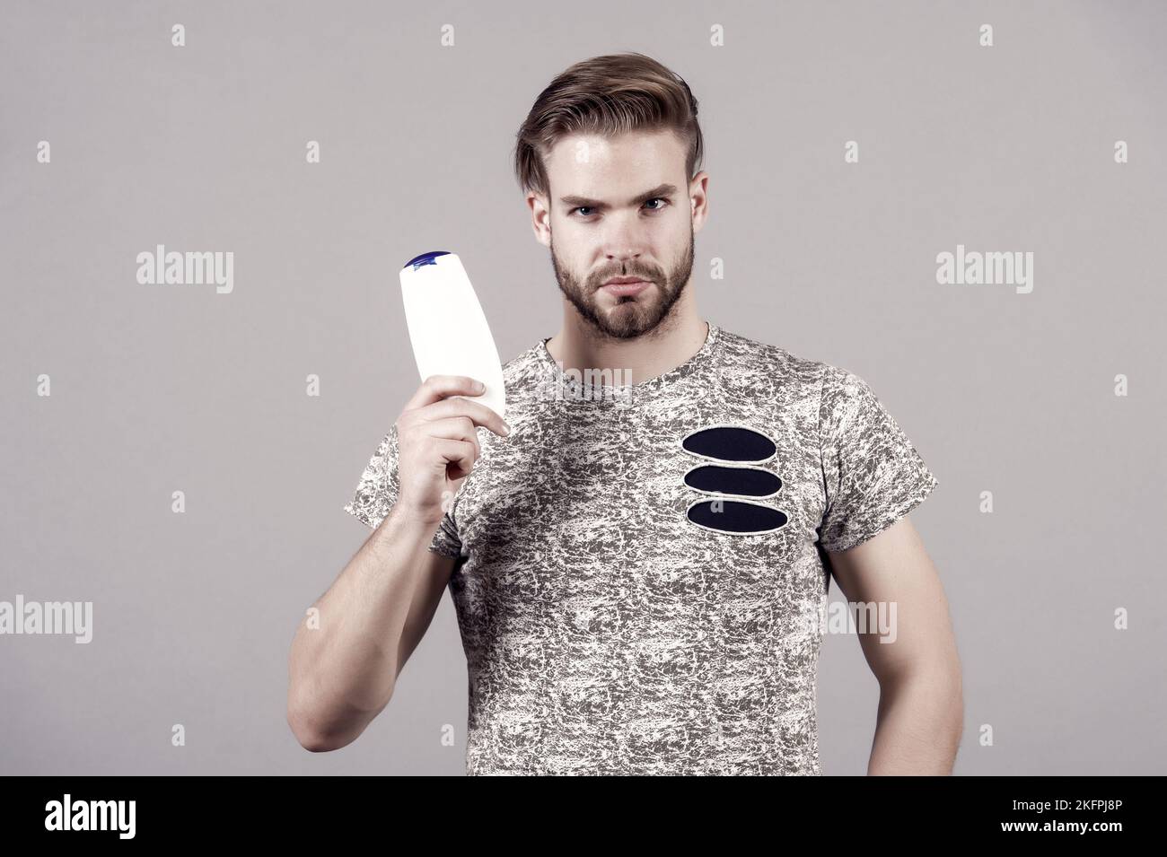 Man strict face holds shampoo bottle, grey background. Man enjoy ...