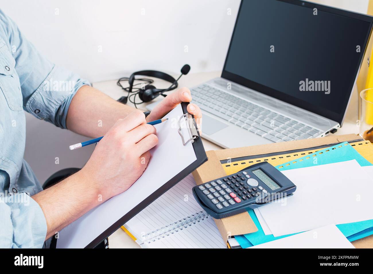 A person writing on a notepad with a laptop, a calculator, papers and ...