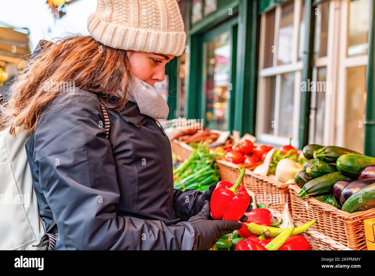 A selective focus of young woman in winter clothes buying peppers and ...