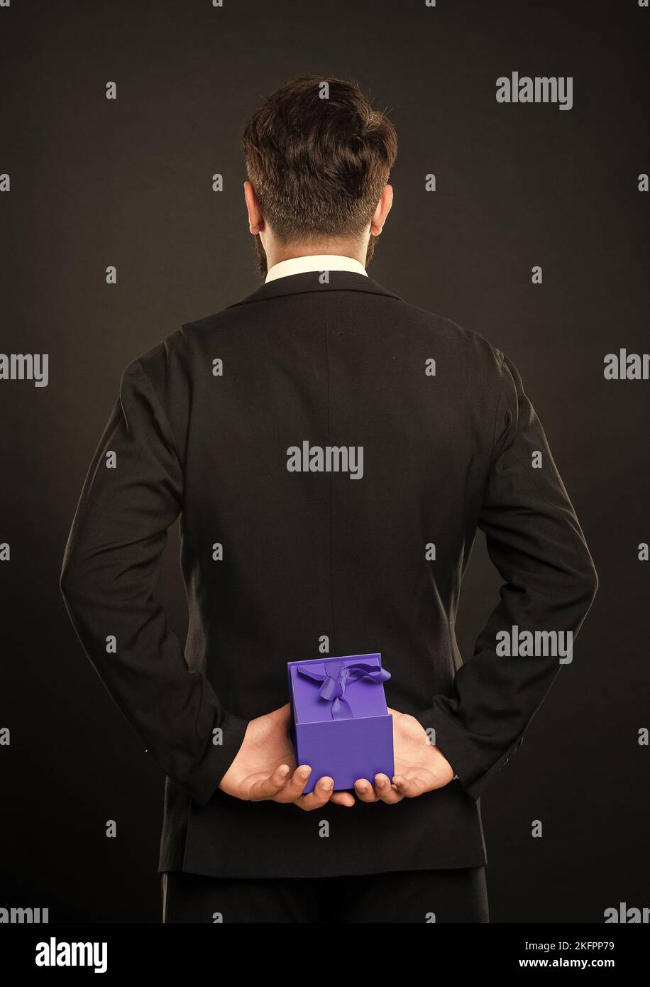 back view of man in tuxedo suit on black background with box. birthday ...