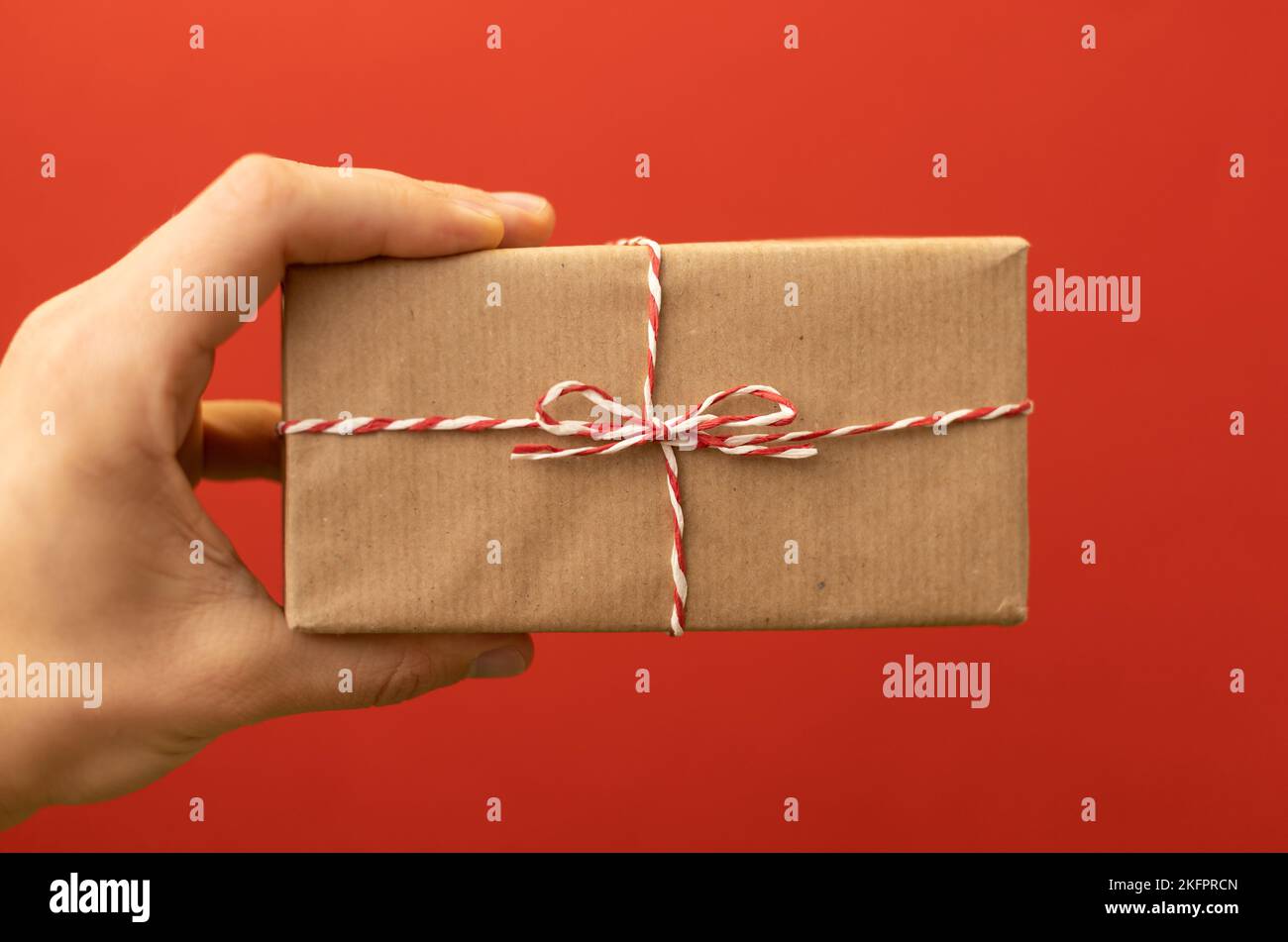 hand holding craft wrapped gift over red background Stock Photo - Alamy