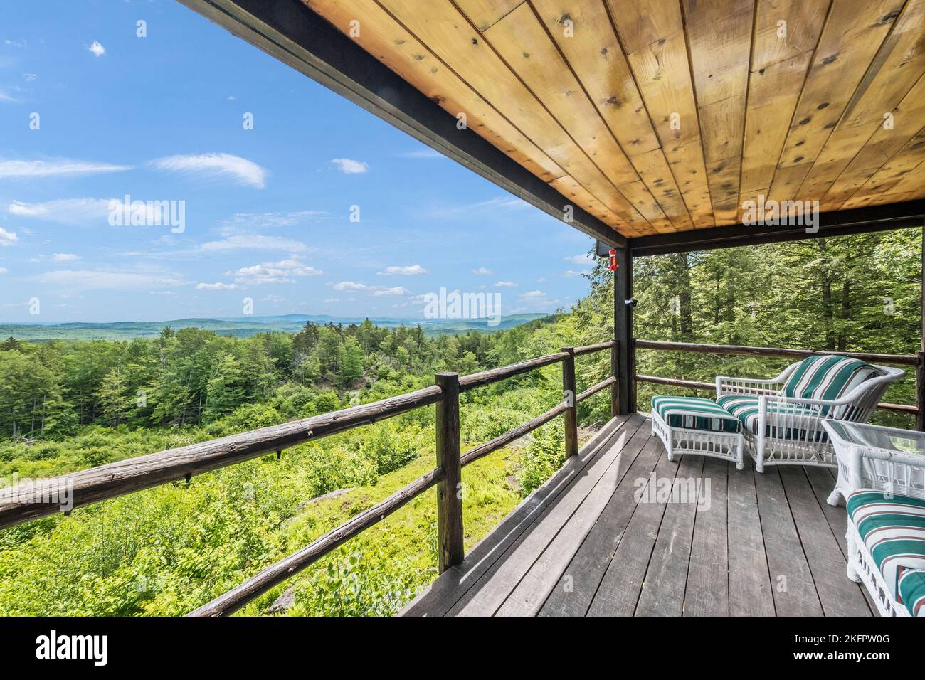 A cabin balcony view of greenery with blue sky and small white clouds ...