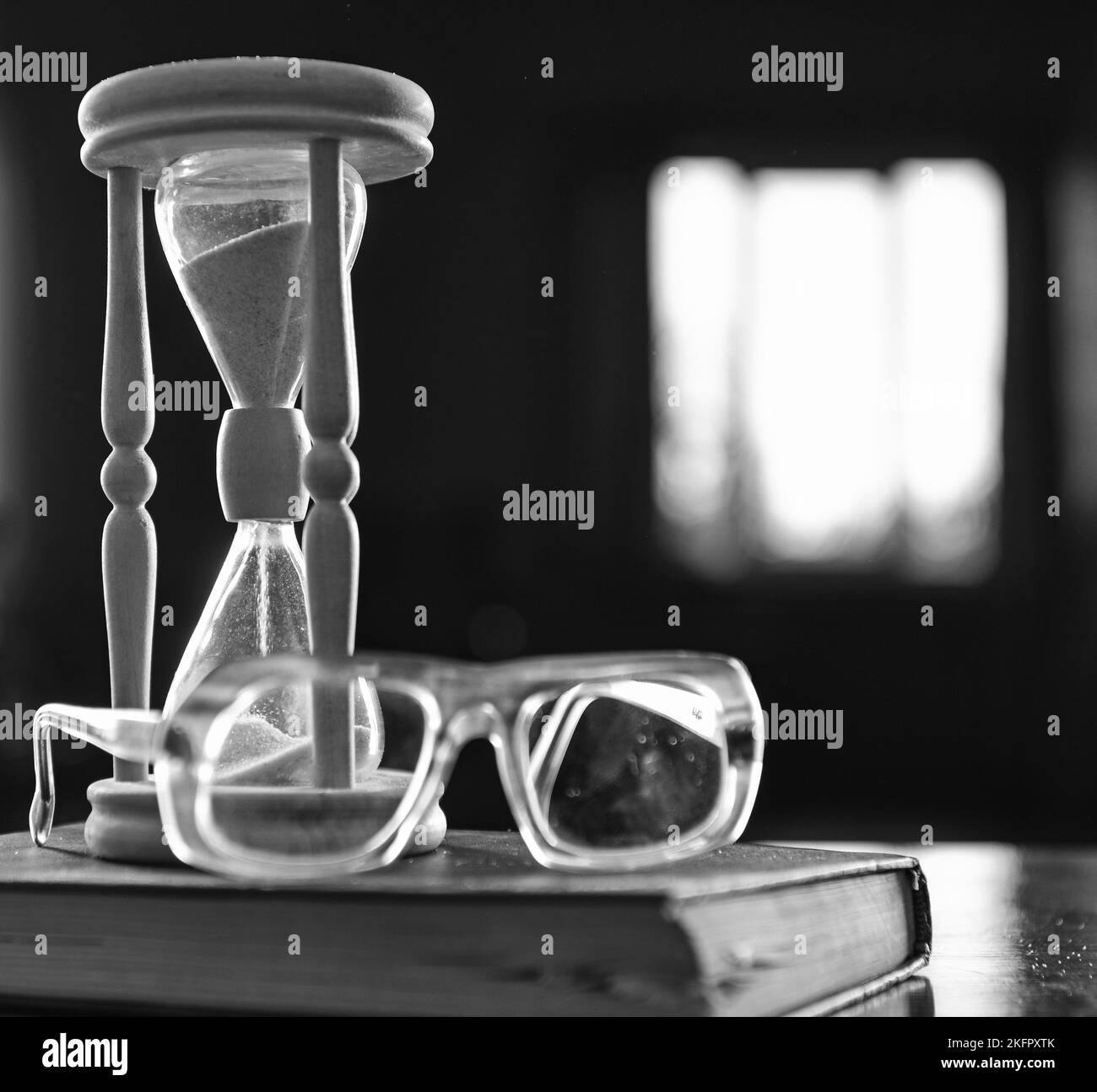 Hourglass, old book and eyeglasses on wooden table, dark background ...