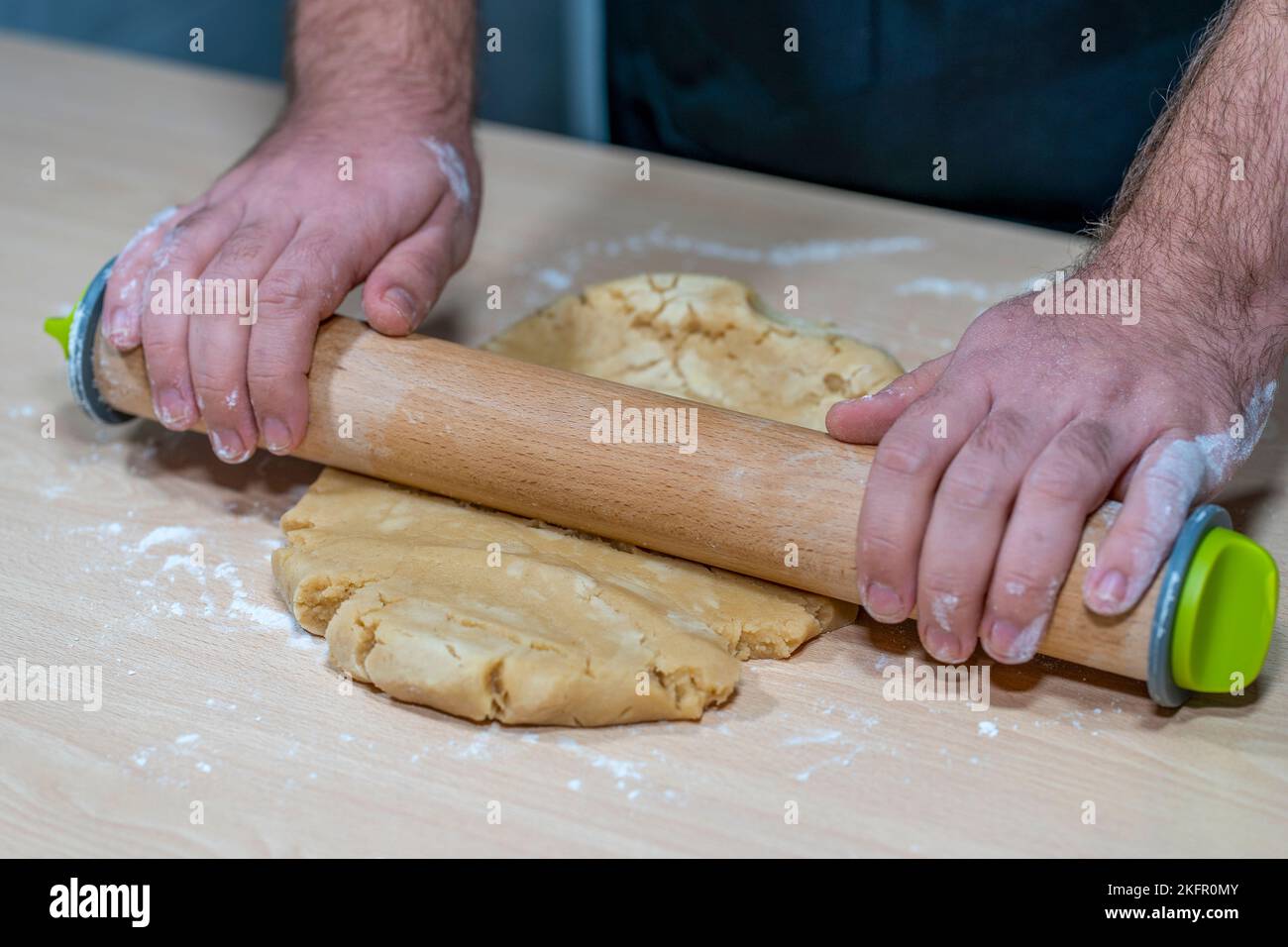 young man kneading with a rolling pin the dough of cinnamon and vanilla ...