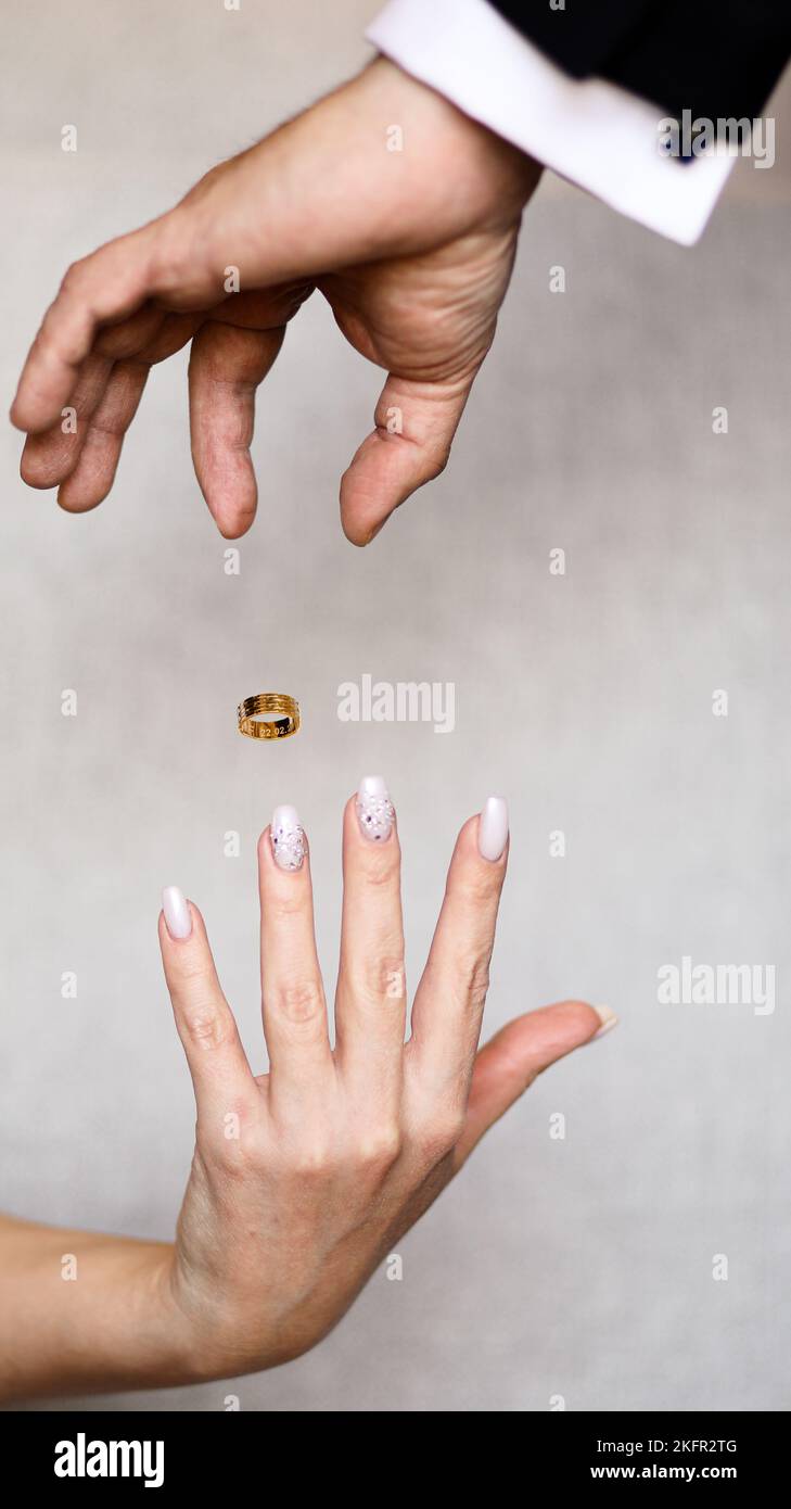 A vertical shot of a groom's hand dropping a gold wedding band onto a ...