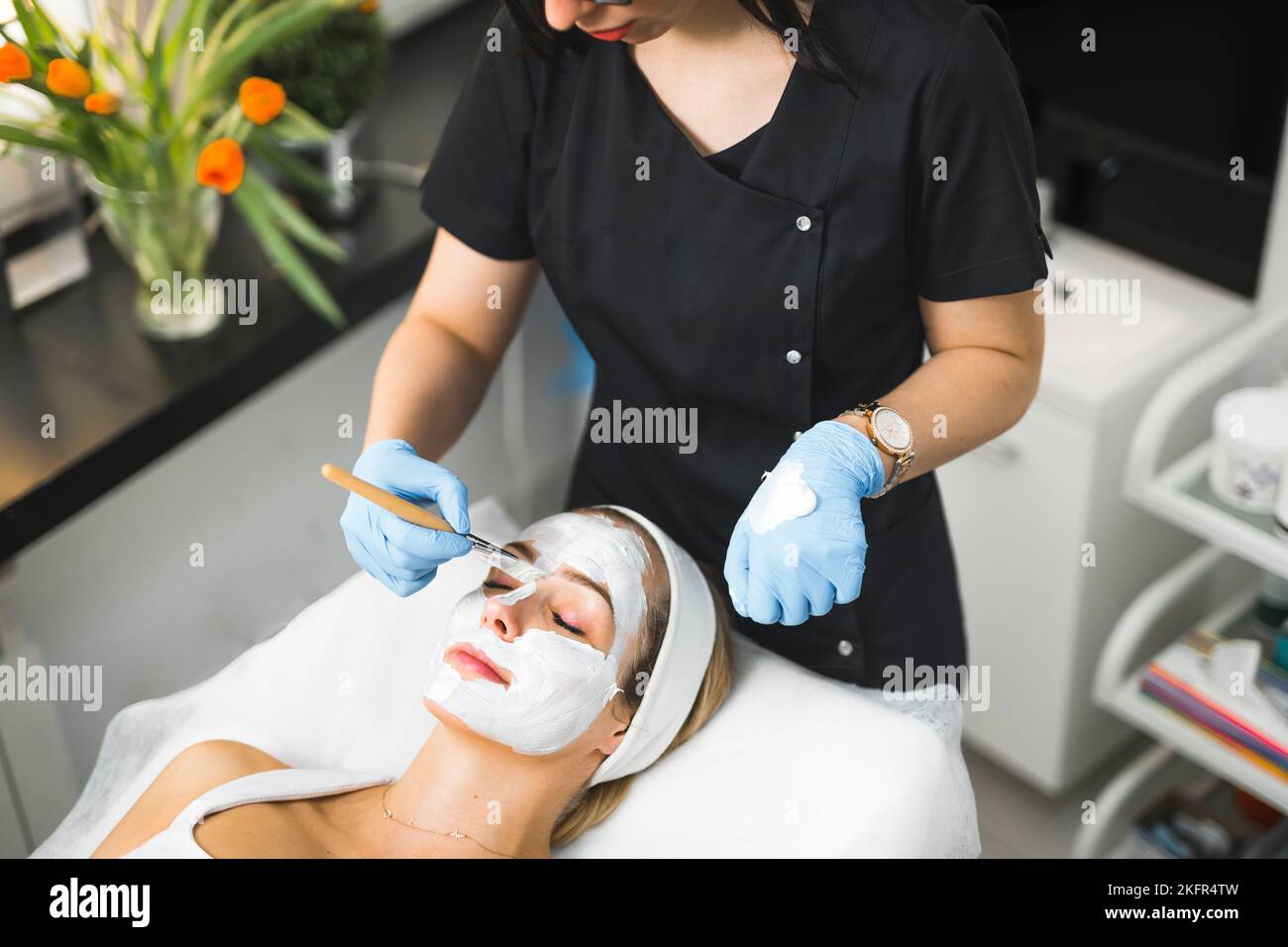 Expert cosmetologist spreading white anti-aging clay mask all over the ...