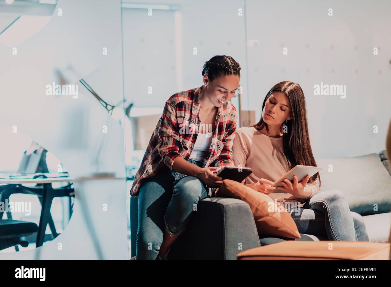 Two young women in a modern office solve a problem together while using ...