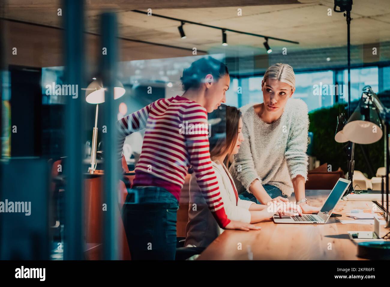 Three young women in a modern office solve a problem together while ...