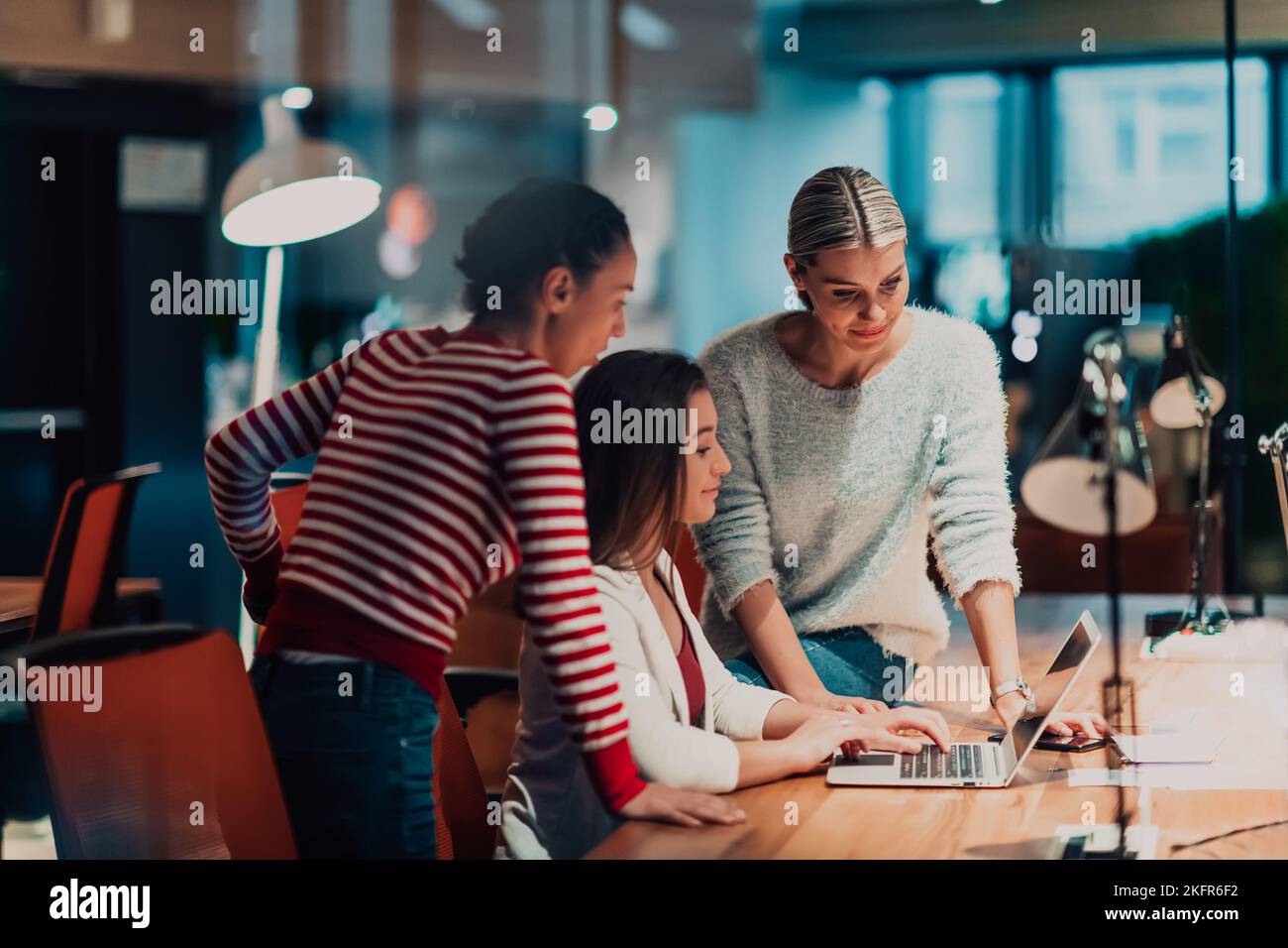 Three young women in a modern office solve a problem together while ...
