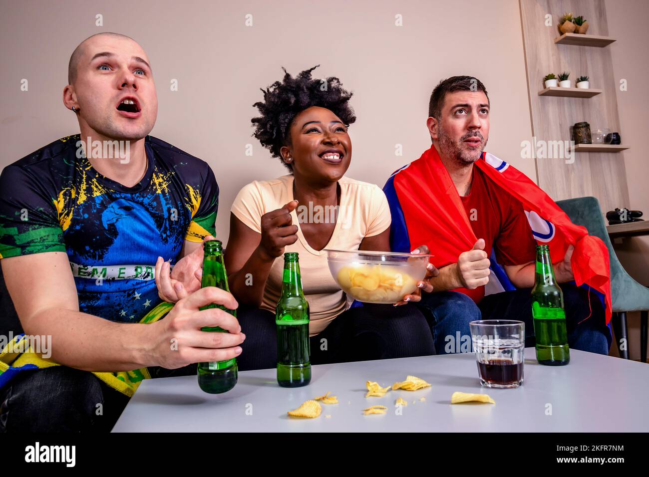 Friends watching a football match on TV, drinking beer and eating chips ...