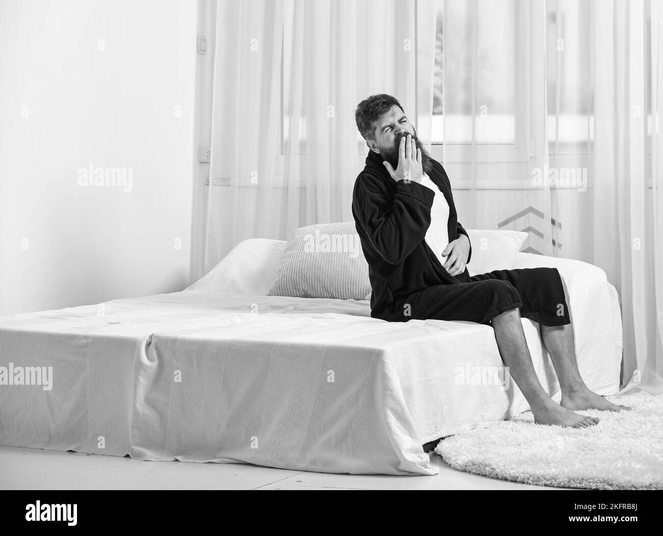 Sleepy young man sitting and yawning in bed at home. Awakening concept ...