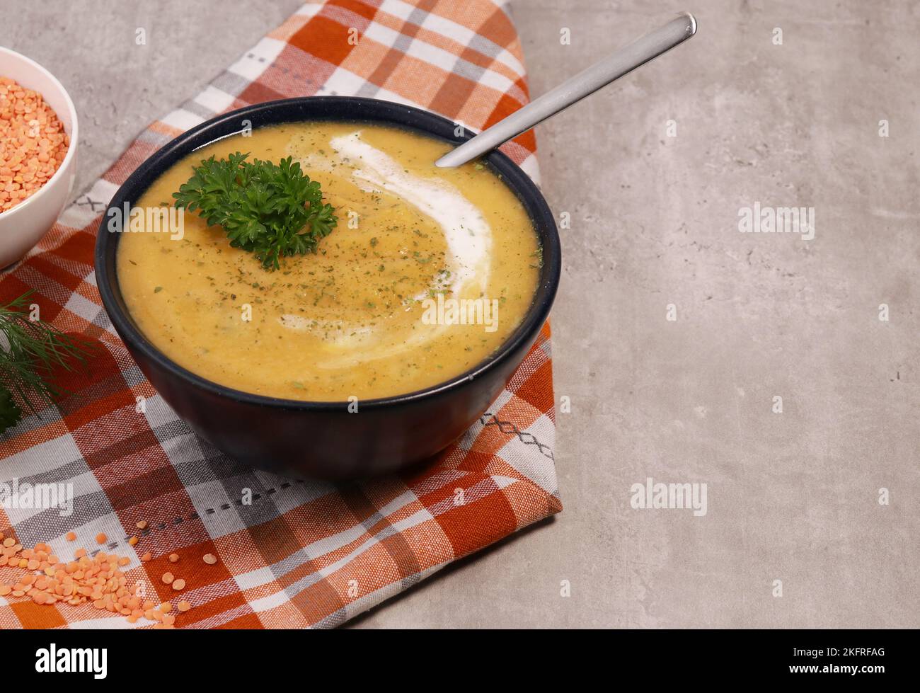 red lentils soup puree in dark bowl with bread on grey marble table ...