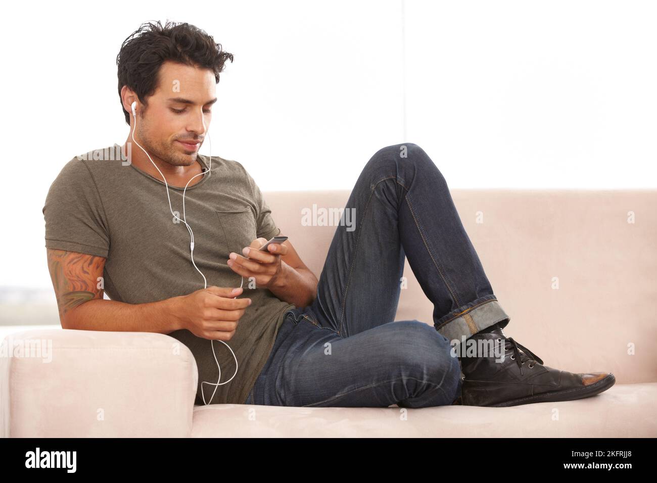 Relaxing with his tunes. A handsome young man relaxing on his sofa and ...