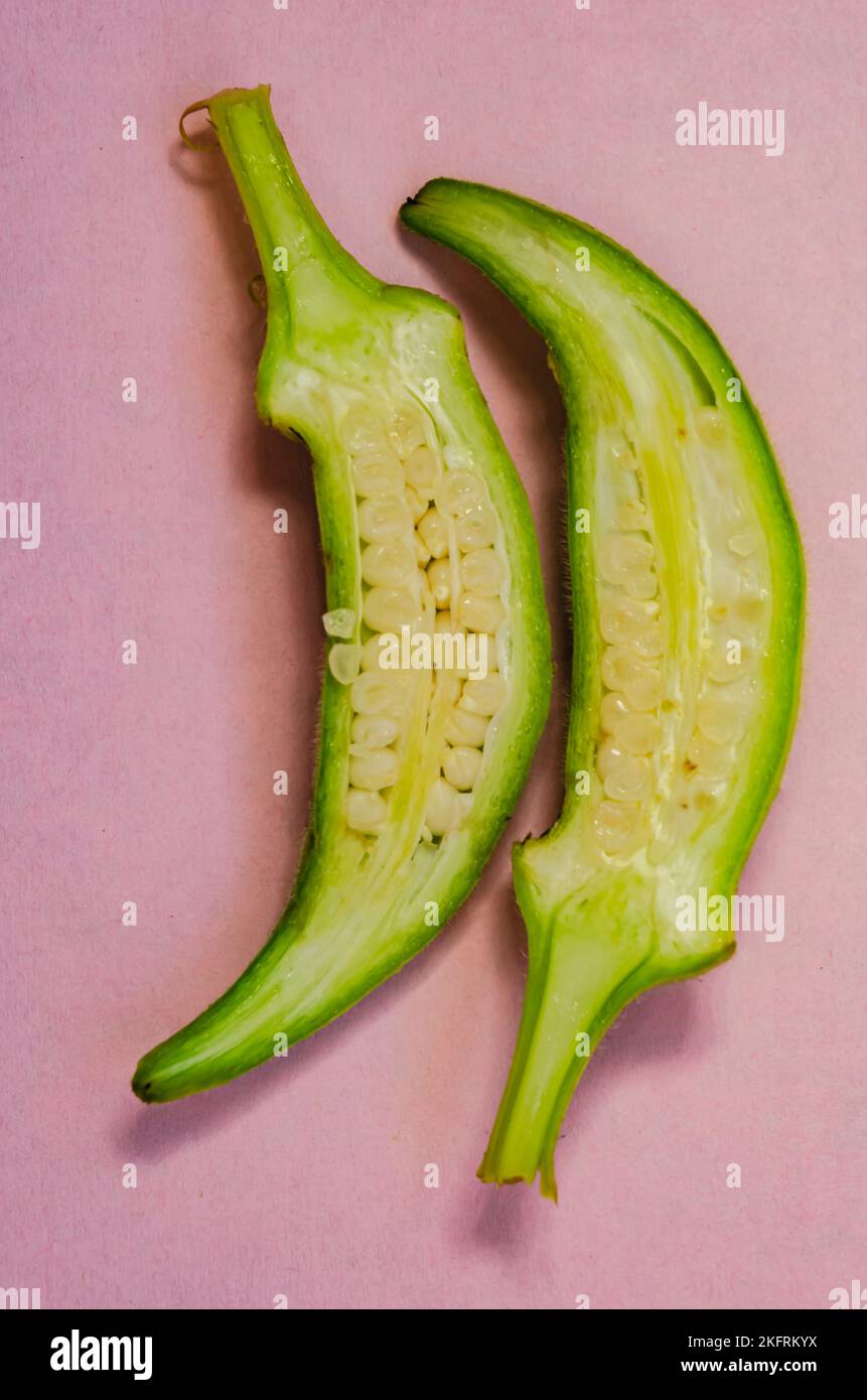 A small okra on a pink background is sliced into halves with its cross ...
