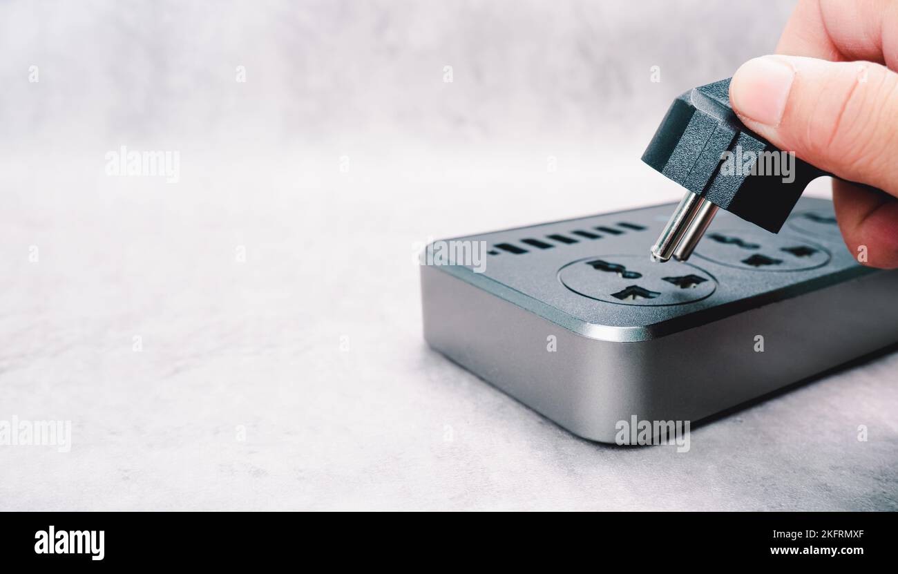 A human hand inserting a plug into a power outlet on the cement floor ...
