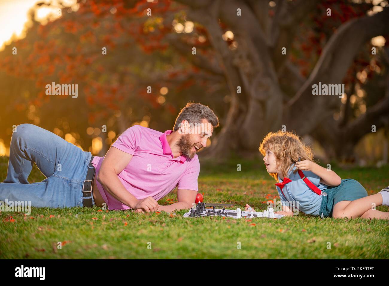 Father and son playing chess lying on grass at lawn park. Fathers Day ...