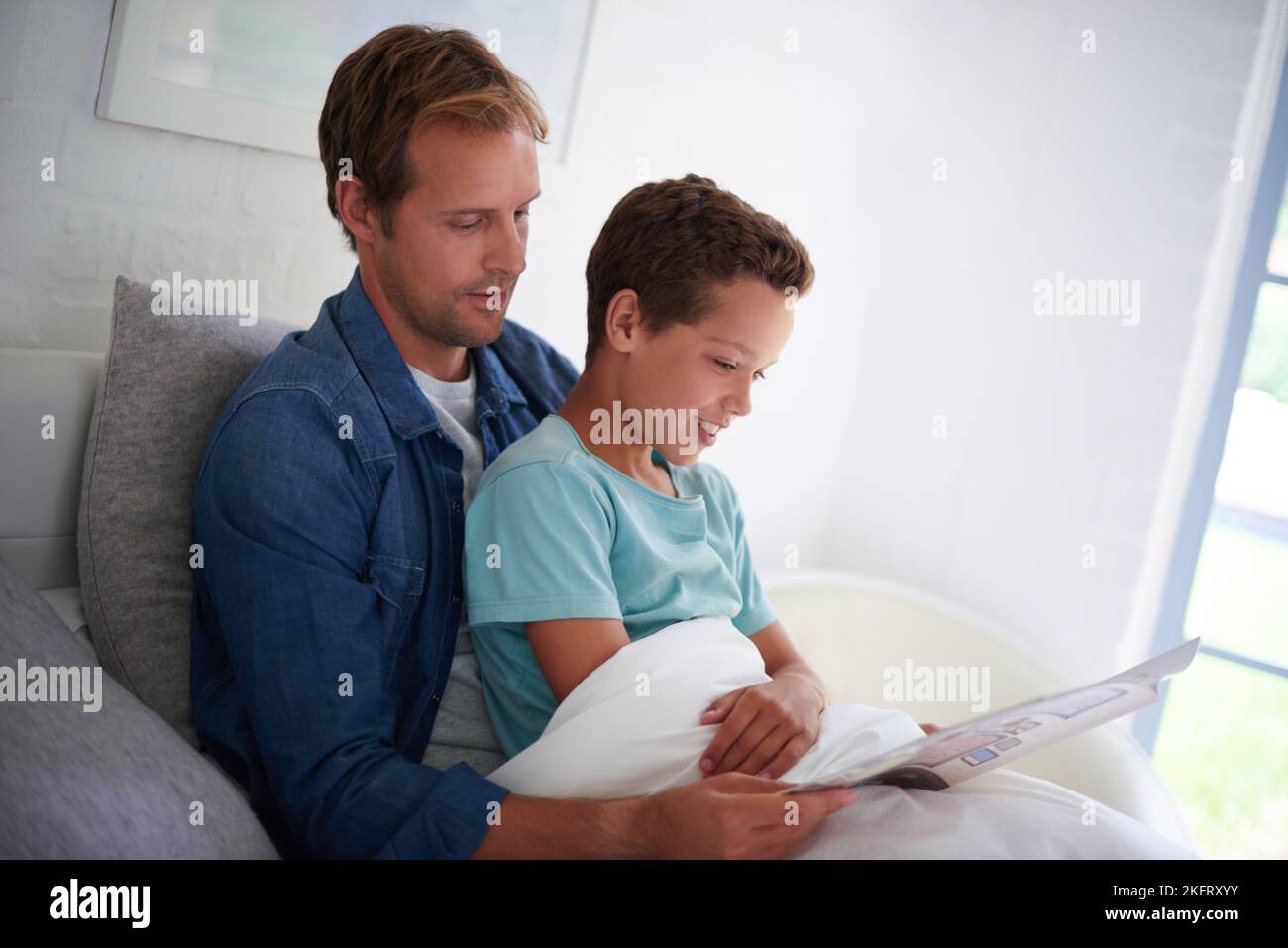 Bedtime bonding with my boy. A father reading a book to his son in bed ...