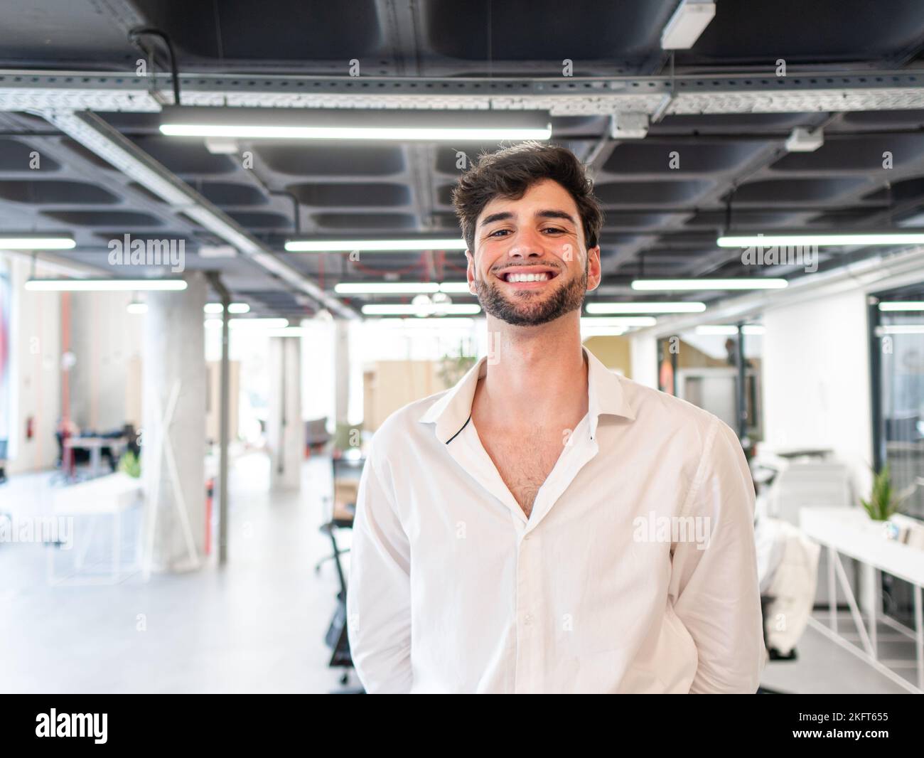 Smiling young bearded man in smart casual outfit standing near table in ...