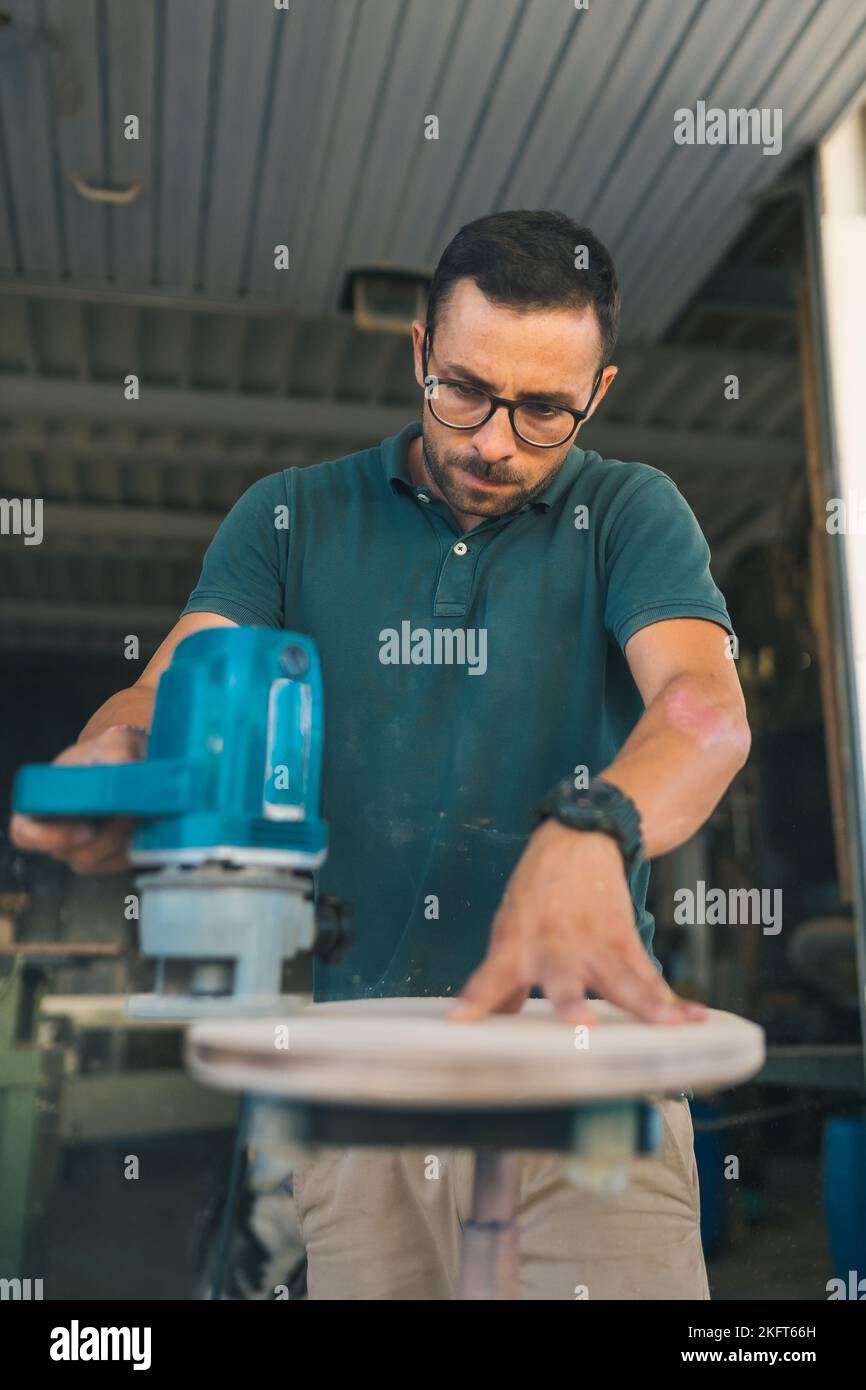 Focused male carpenter in casual clothes cutting wood with milling ...