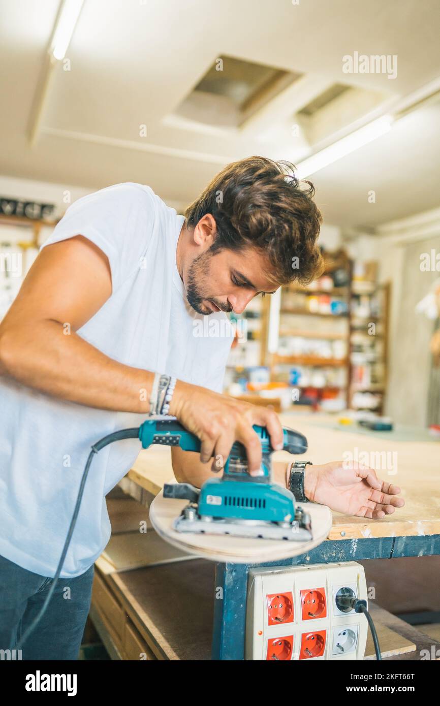 Male carpenter using electric sander to polish wooden plank in joinery ...