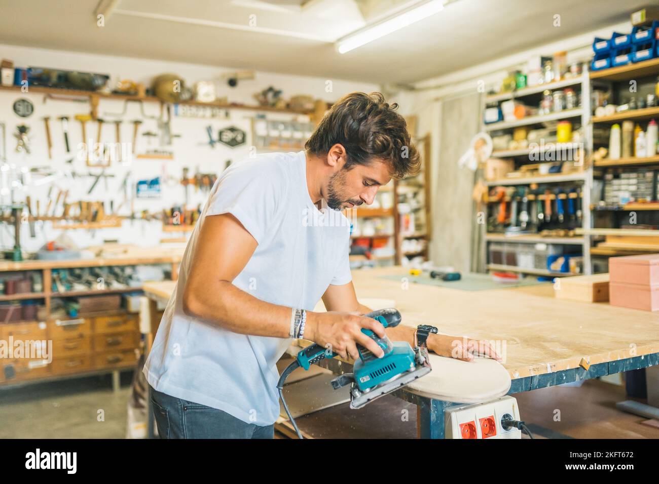 Male carpenter using electric sander to polish wooden plank in joinery ...