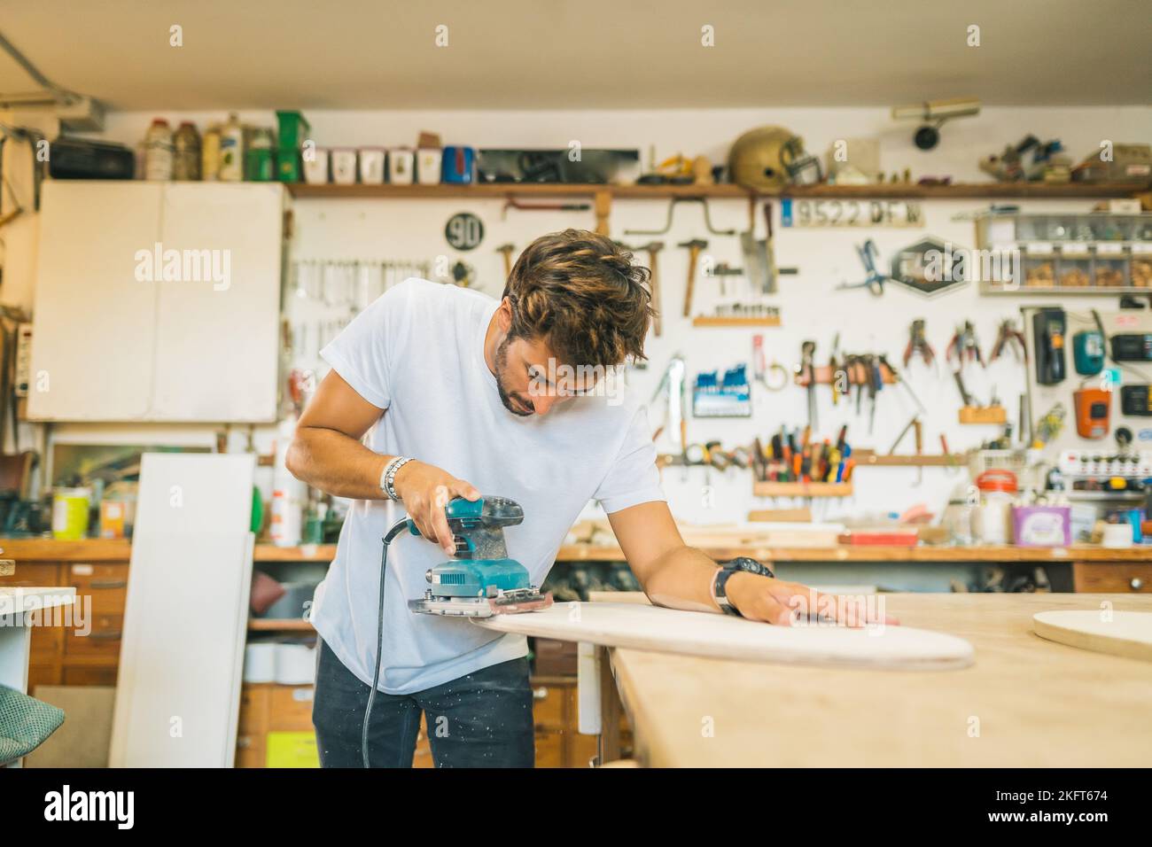 Male carpenter using electric sander to polish wooden plank in joinery ...