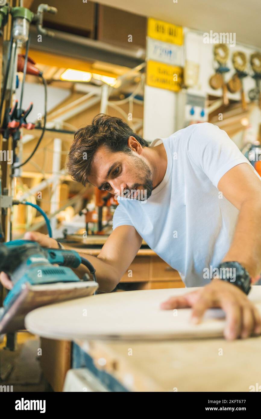 Male carpenter using electric sander to polish wooden plank in joinery ...