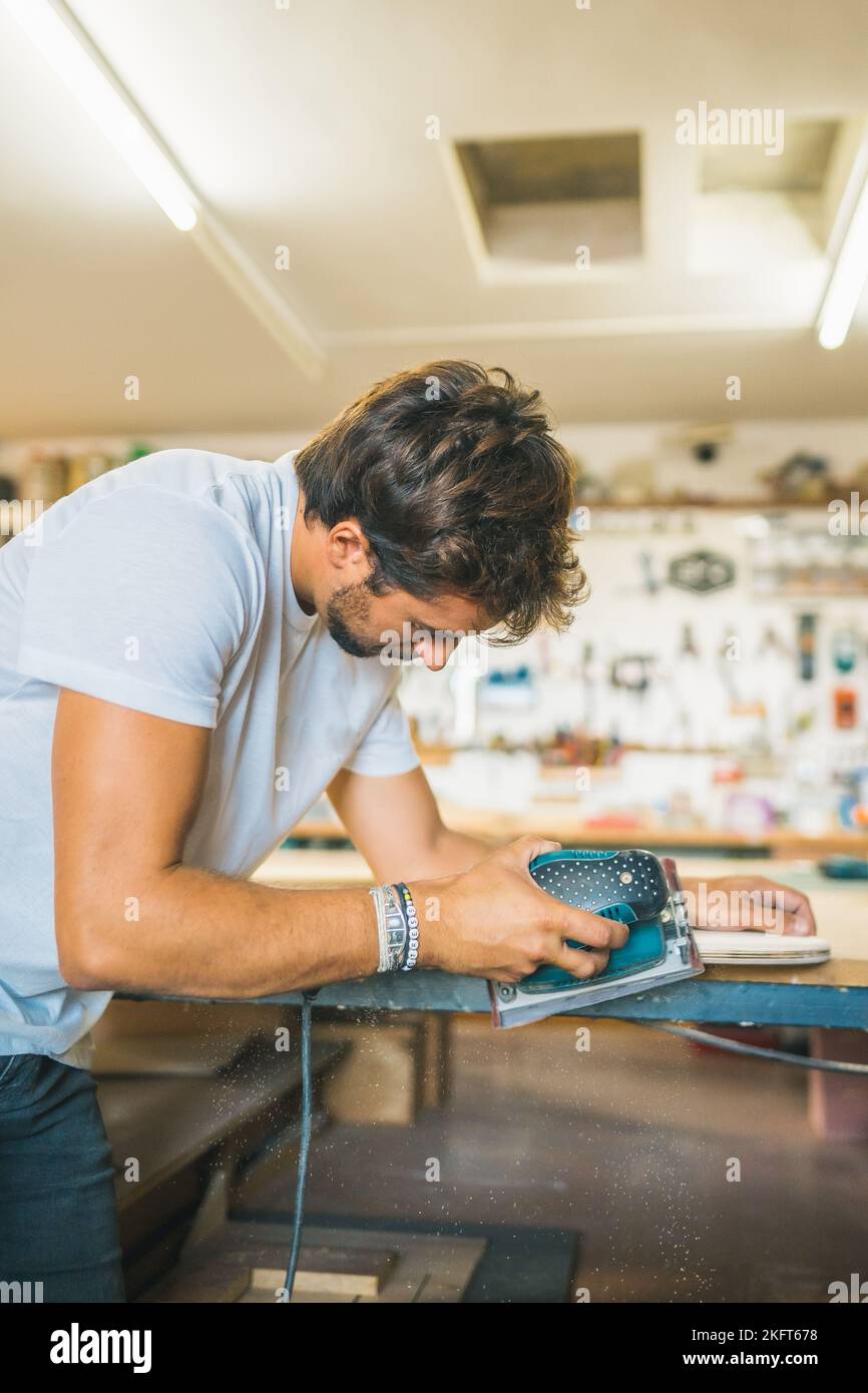 Male carpenter using electric sander to polish wooden plank in joinery ...