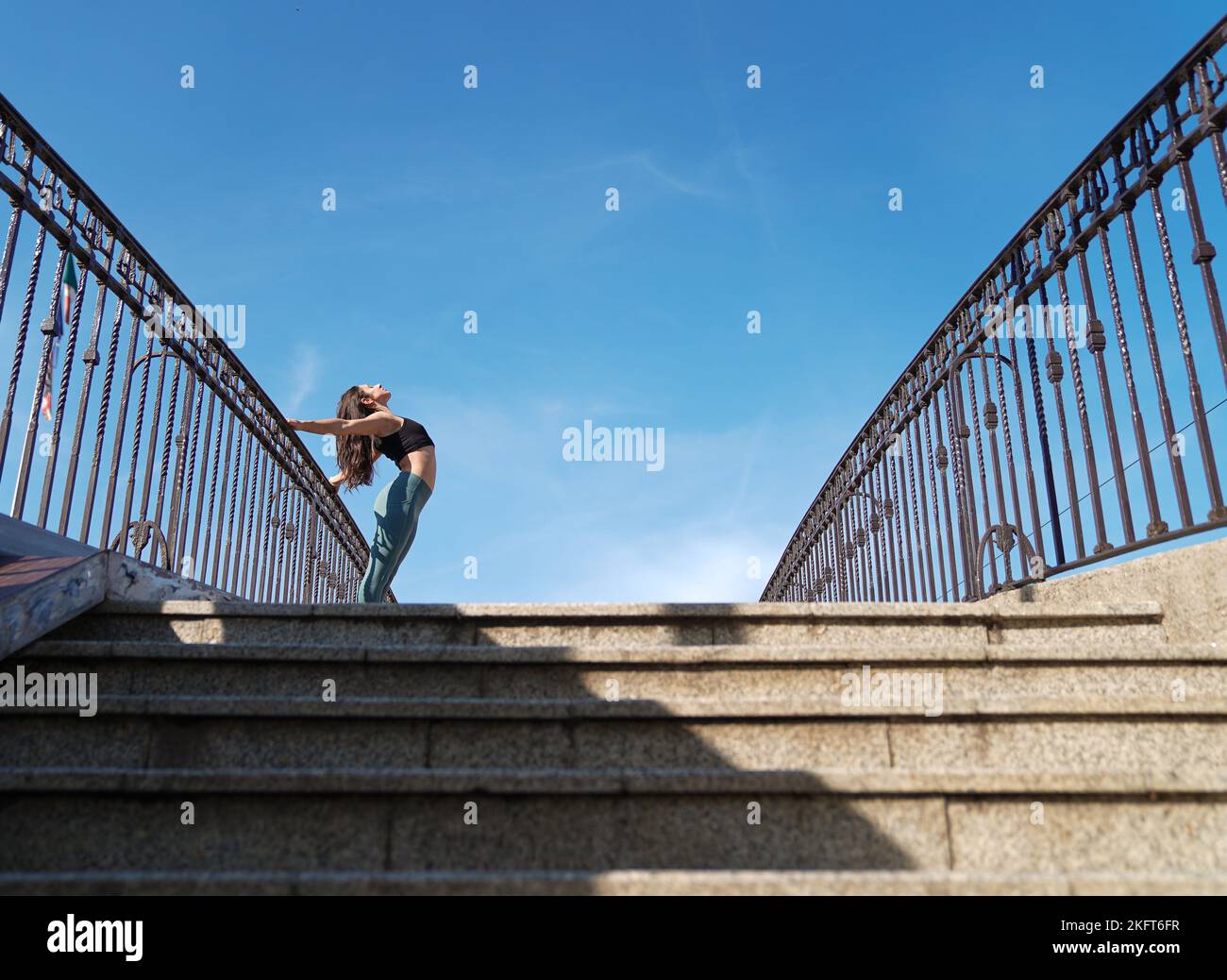 Low angle side view of young female athlete in sportswear stretching on ...
