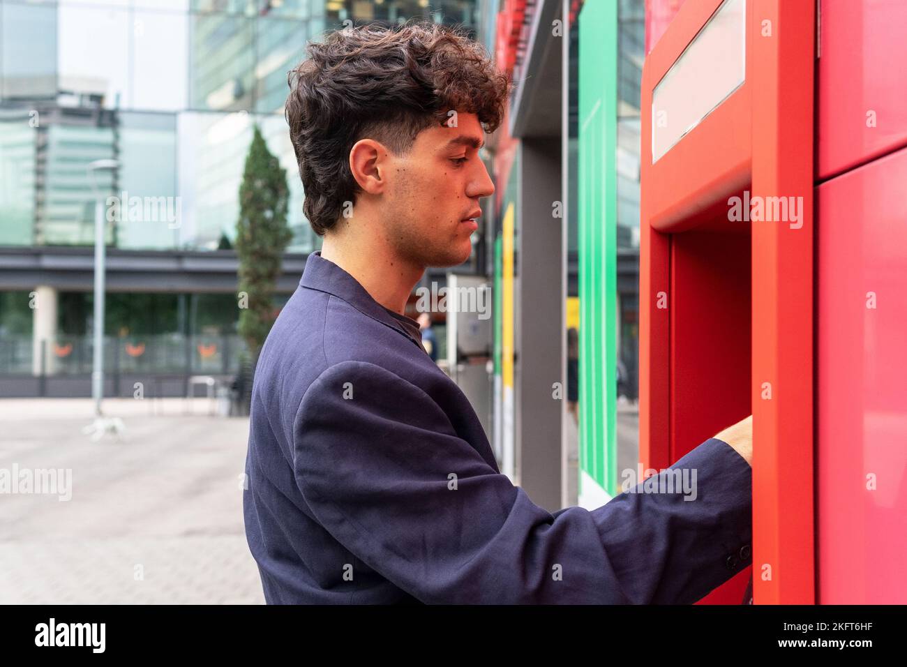 Side view of male using ATM control panel on city street Stock Photo ...