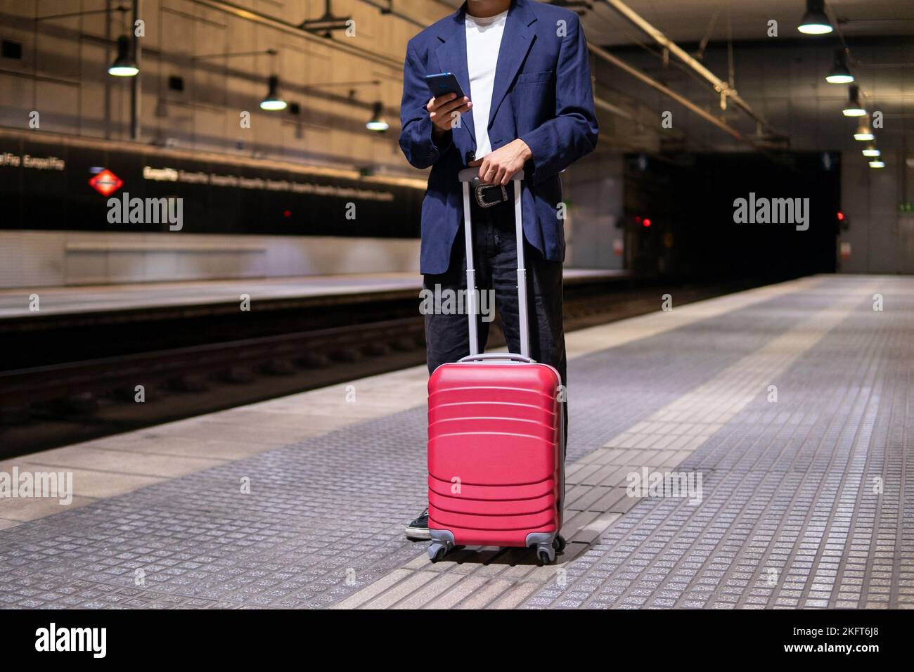 Anonymous young man in smart casual clothes with suitcase using ...