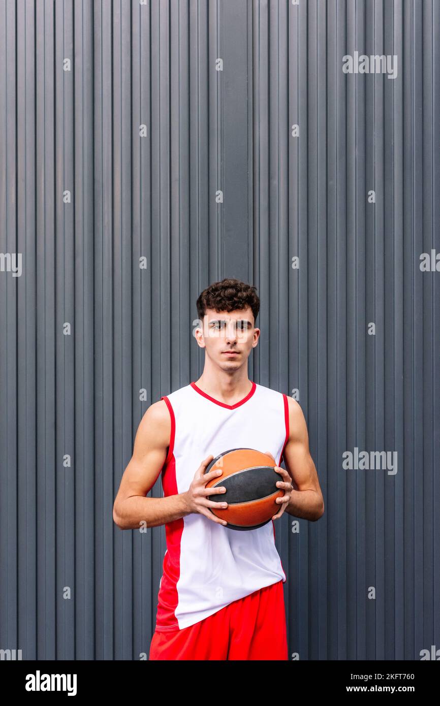 Portrait of serious man in activewear with ball standing against dark ...
