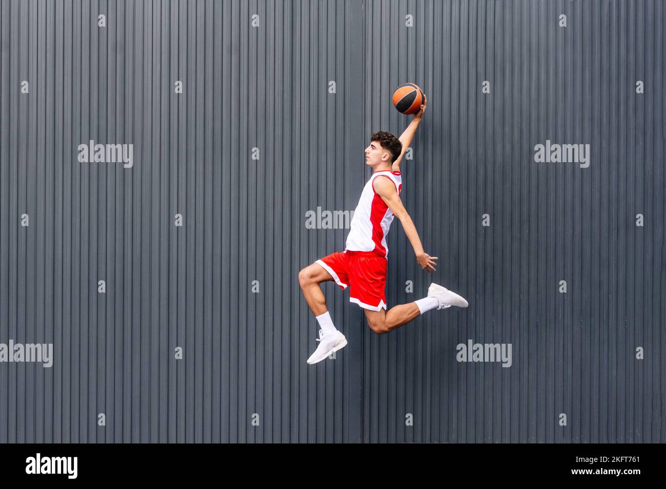 Full body serious man in activewear jumping with ball standing against ...