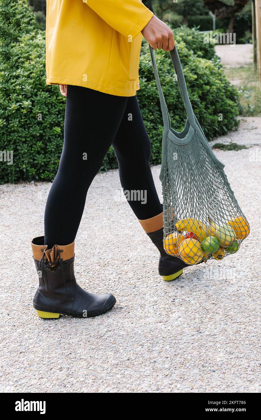 Side view of anonymous female in bright yellow coat strolling in park ...
