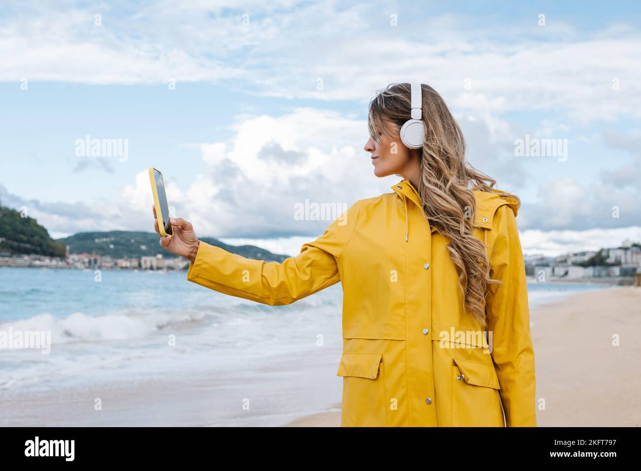 Young female in yellow raincoat having video call on mobile phone on ...