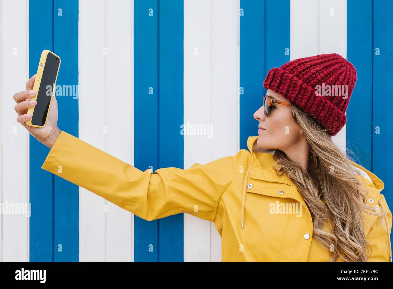 Side view of crop female with long blond hair in yellow raincoat taking ...